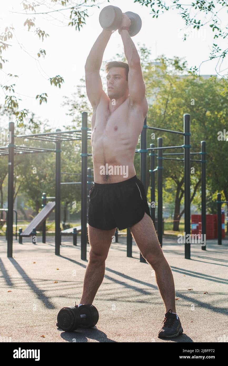 Muscular male athlete with arms raised doing lifting exercises with ...