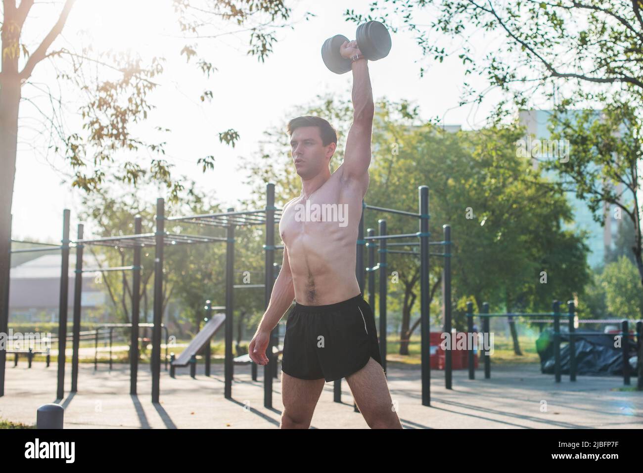 Muscular male athlete with arms raised doing lifting exercises with ...