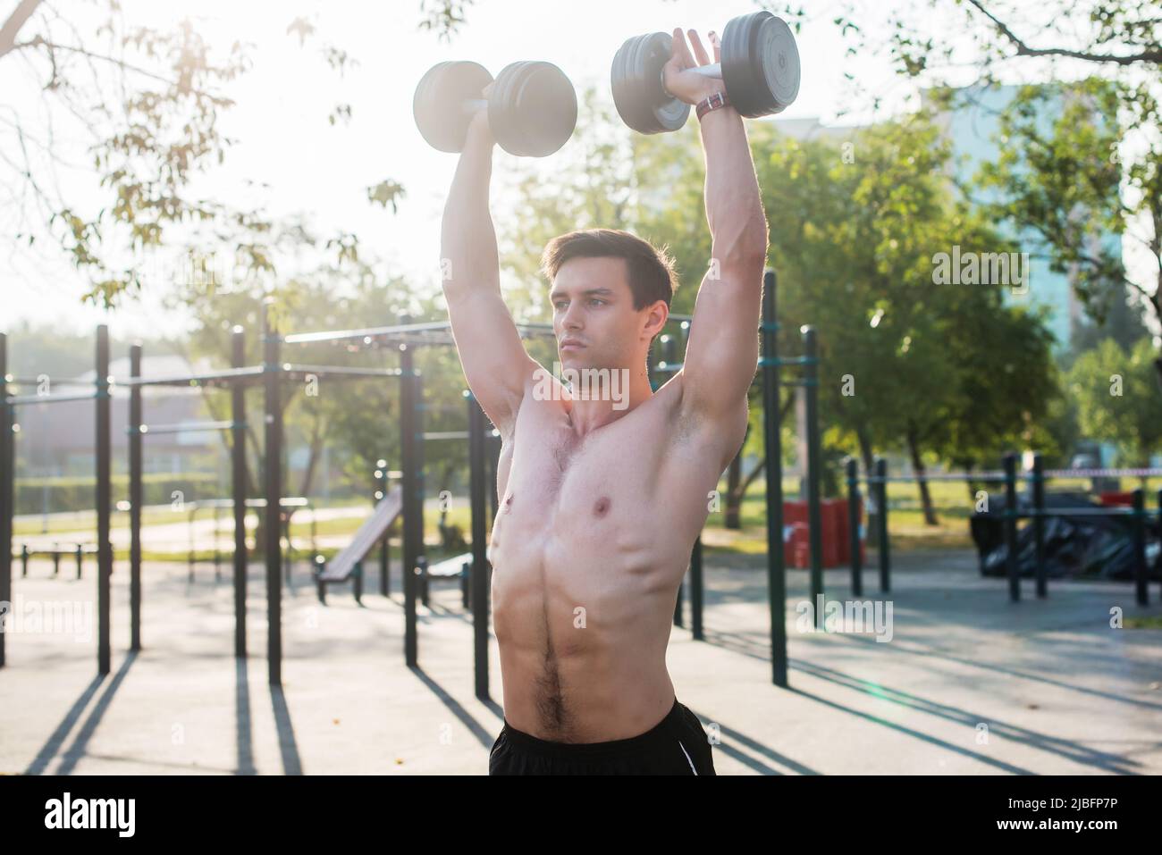 Muscular male athlete with arms raised doing lifting exercises with ...