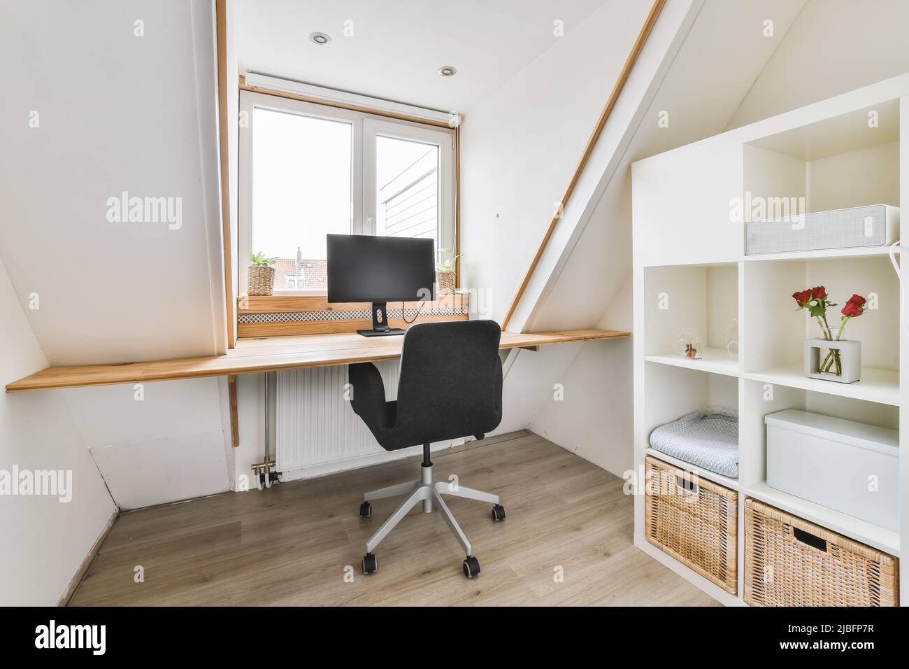 Modern computer placed on wooden desk near shelves decorated with ...