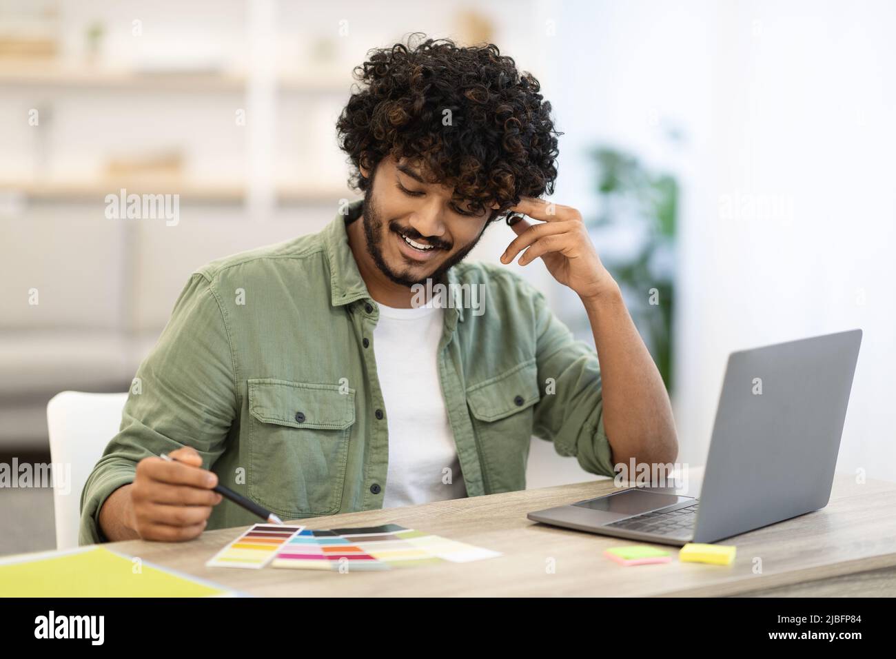 Positive hindu man web designer working on laptop, office interior ...
