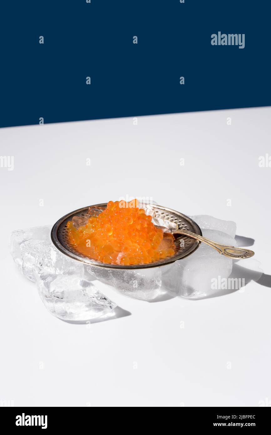 Orange tobiko caviar served on silver plate with ice with spoon on ...