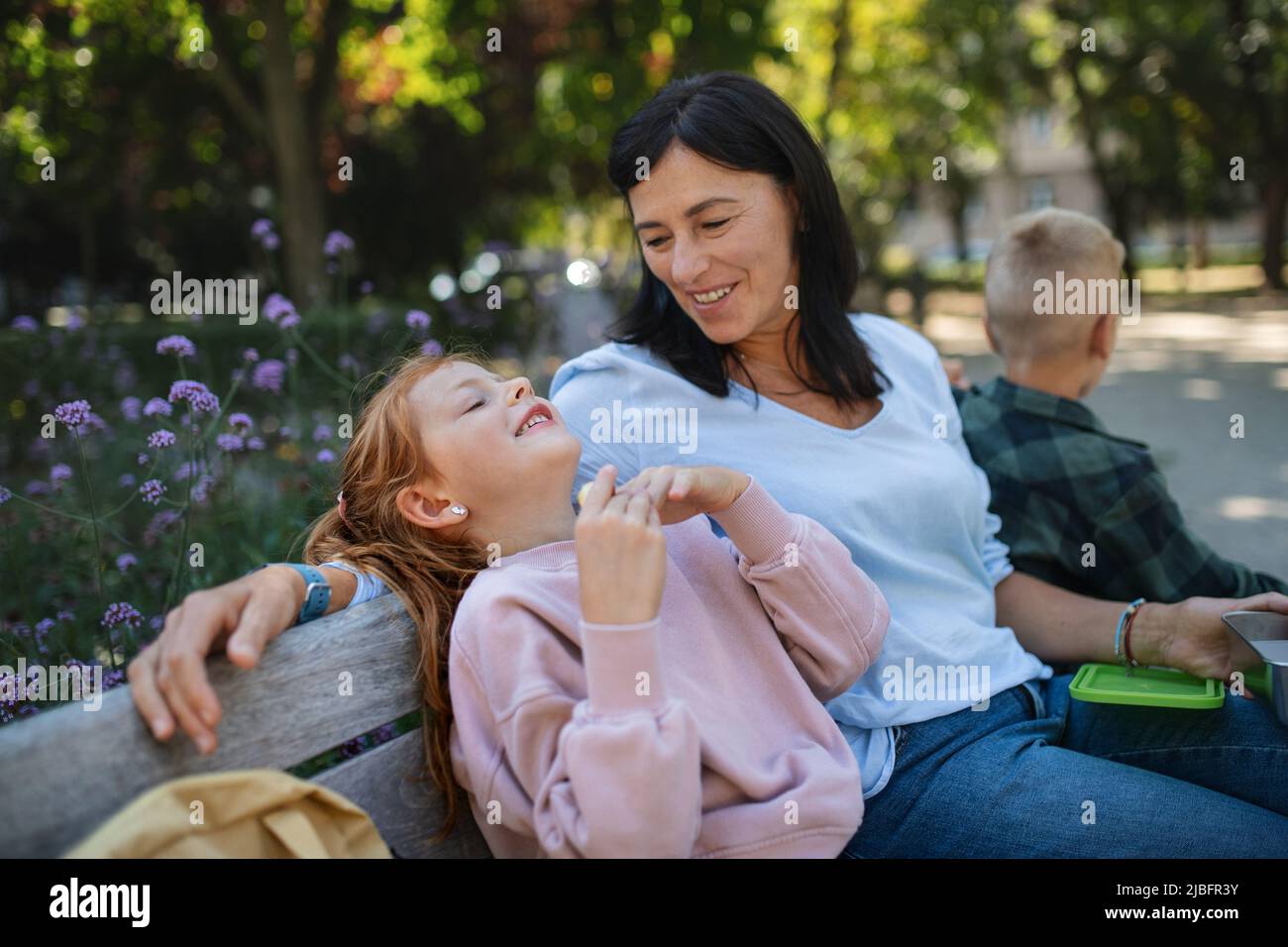 Happy senior woman with grandchildren sitting on bench and having snack ...