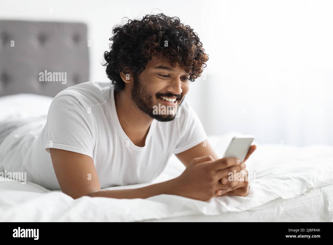 Handsome hindu guy laying on bed with phone, closeup Stock Photo - Alamy