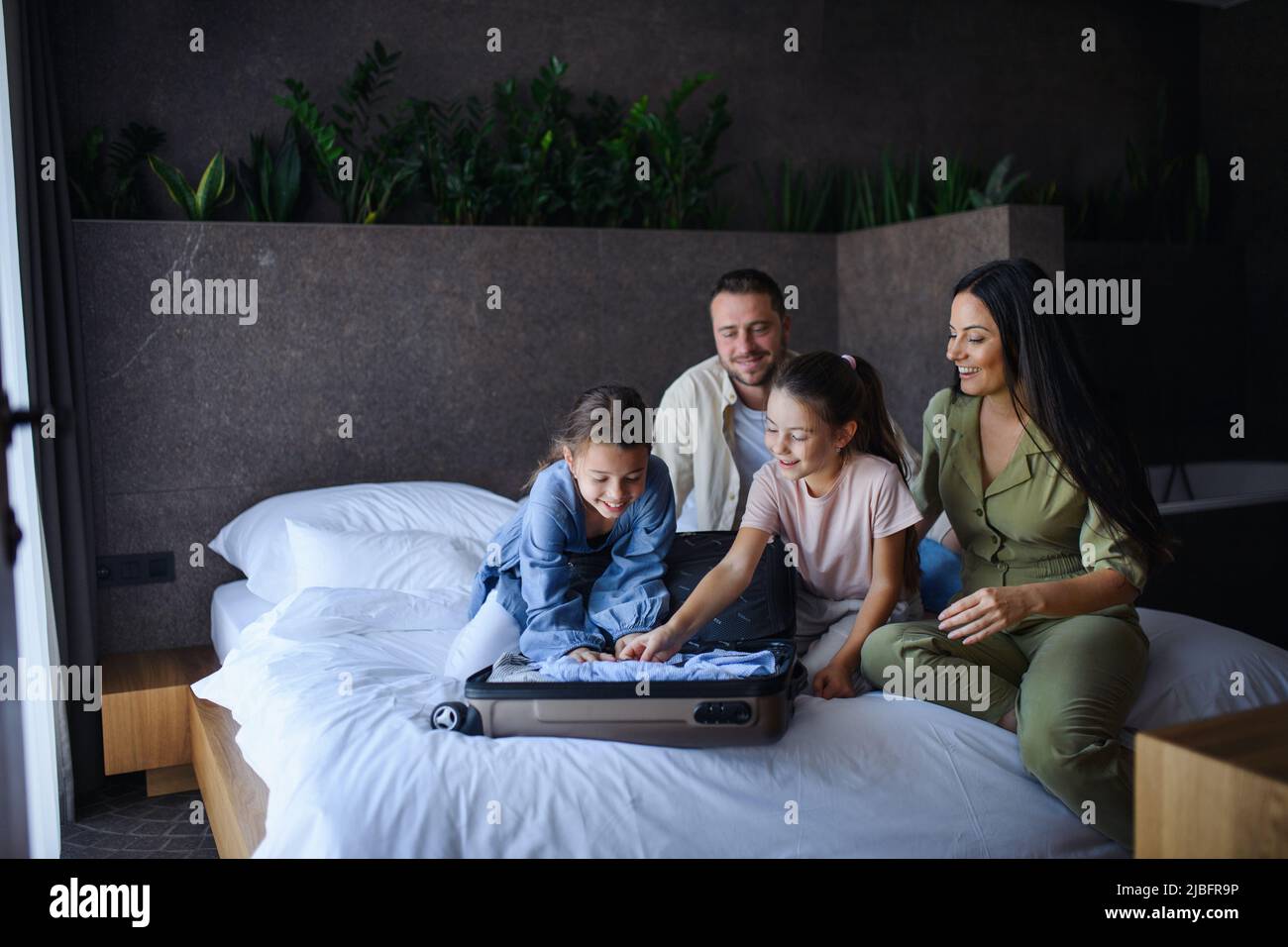 Happy young family with two children sitting on bed and unpacking at ...