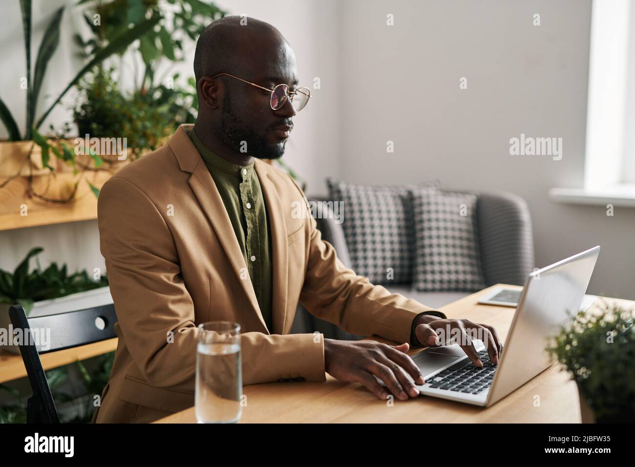Serious young black man in formalwear sitting by workplace in front of ...