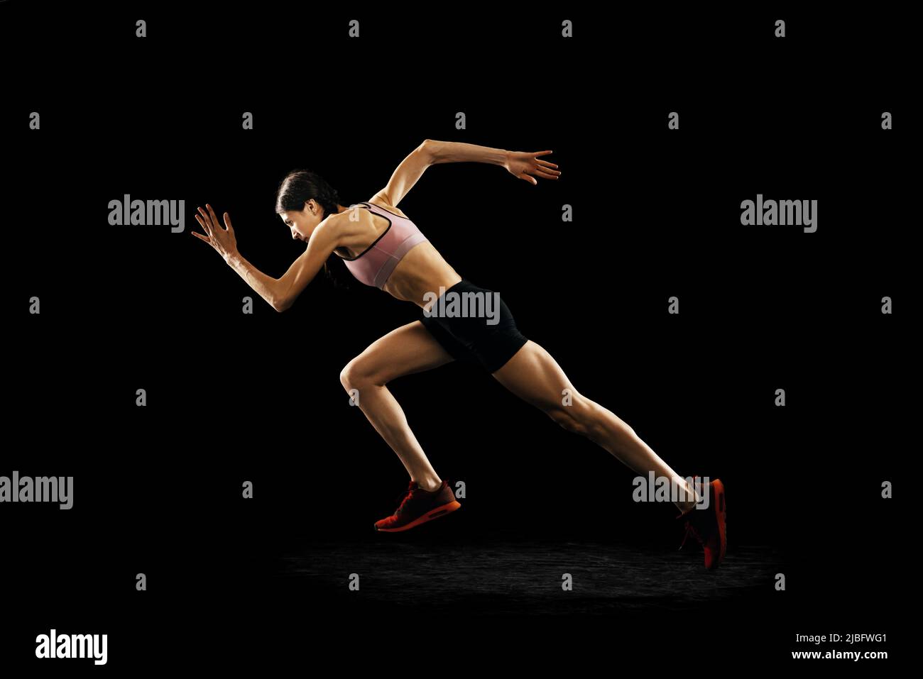 Studio shot of young muscular woman running isolated on black ...