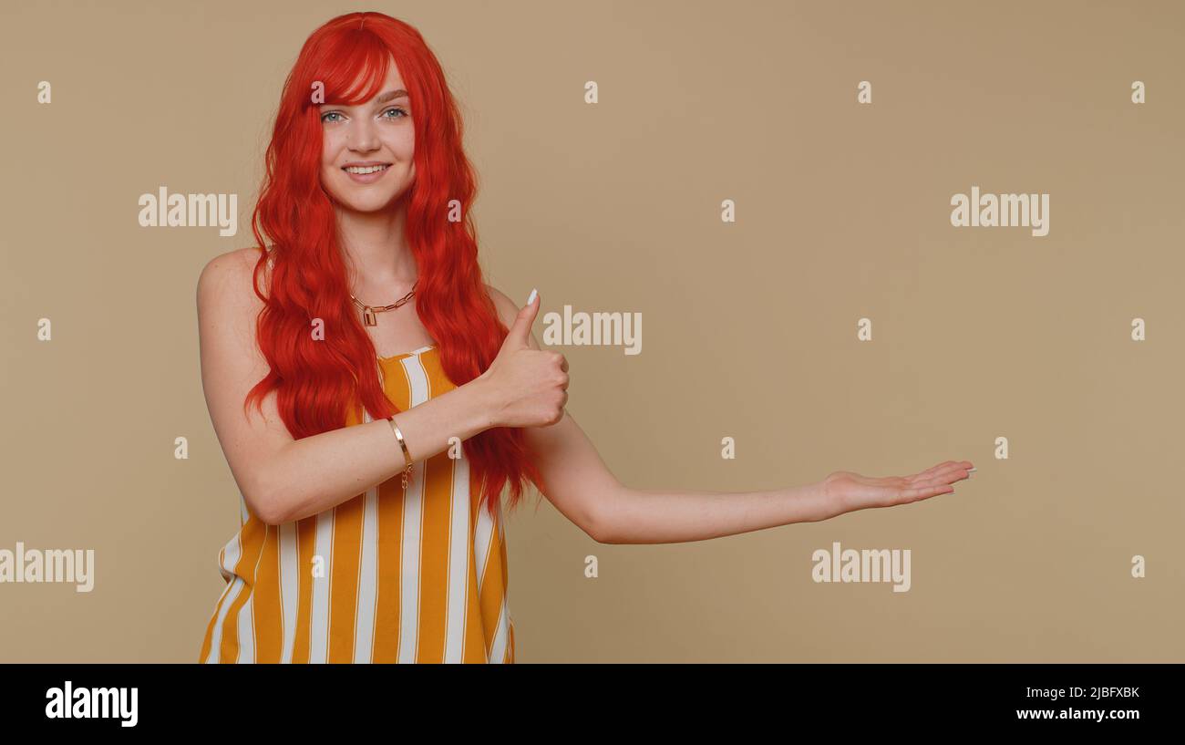 Beautiful redhead woman showing thumbs up and pointing empty place ...