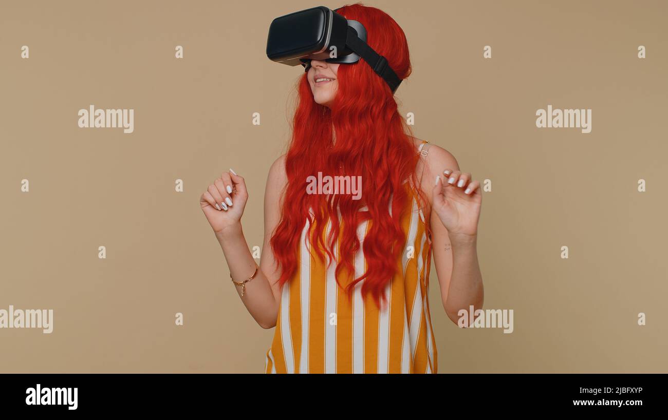 Exited redhead woman using virtual reality futuristic technology VR app ...