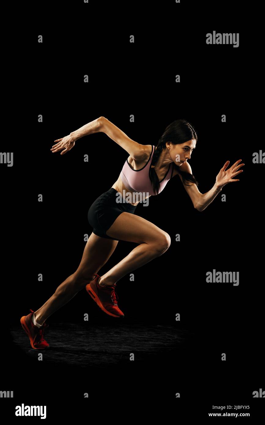 Studio shot of young muscular woman running isolated on black ...
