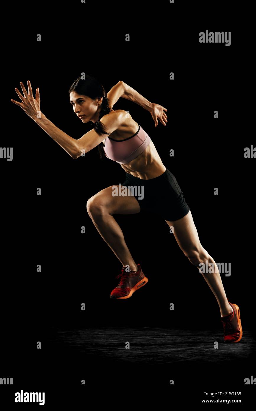 Studio shot of young muscular woman running isolated on black ...