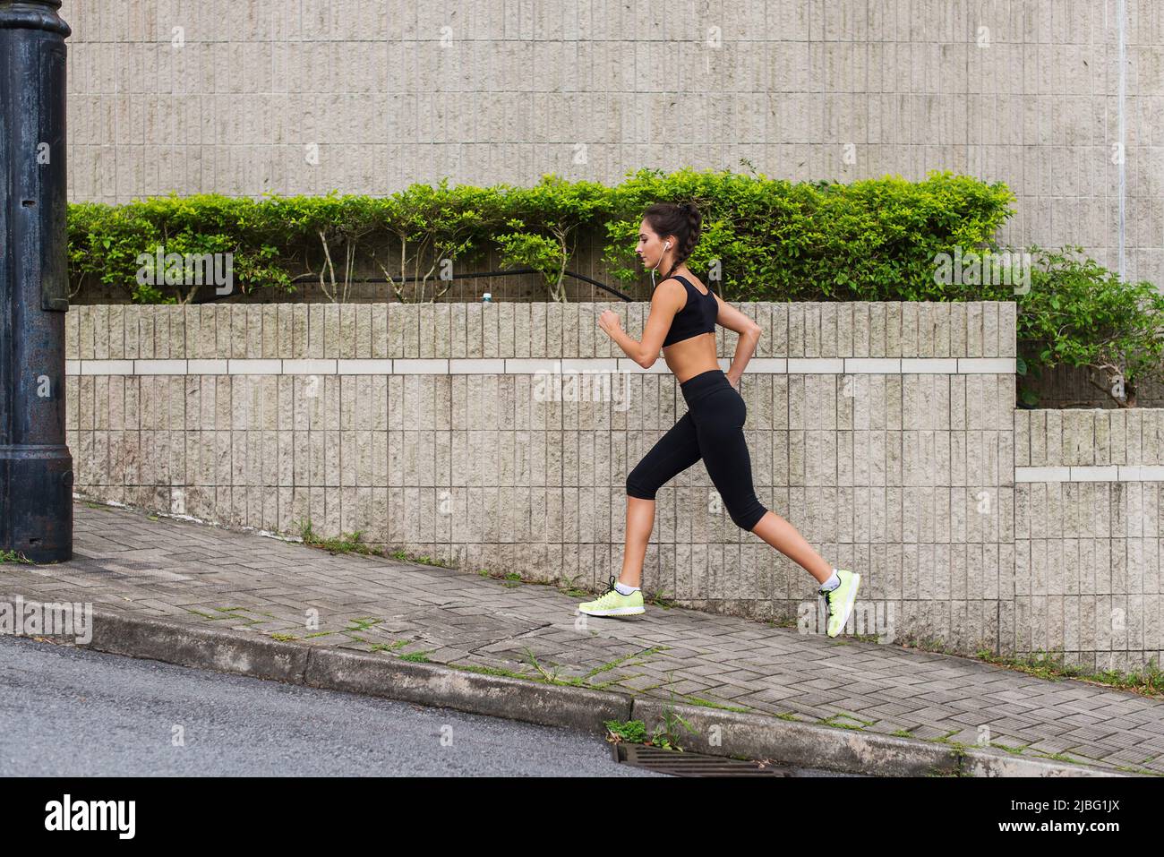 Slim young woman running uphill on sidewalk of city street. Female ...