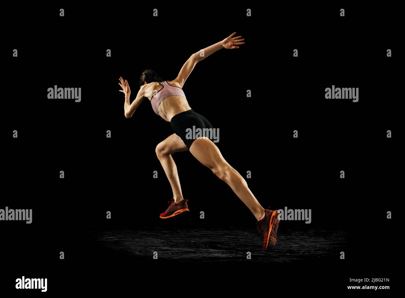 Back view of young muscular woman running isolated on black background ...
