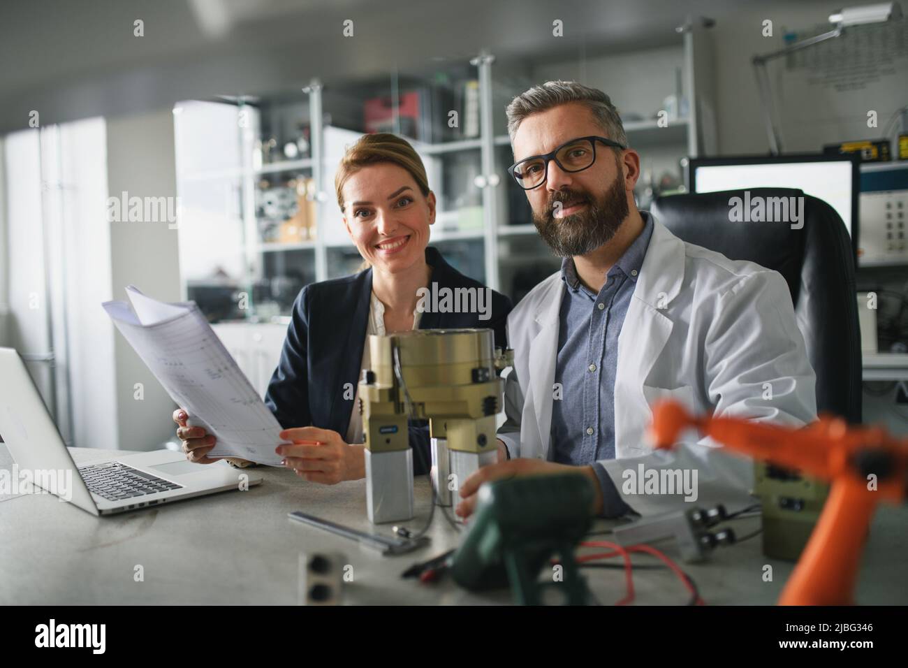 Robotics engineers working on laptop and desinging modern robotic arm ...