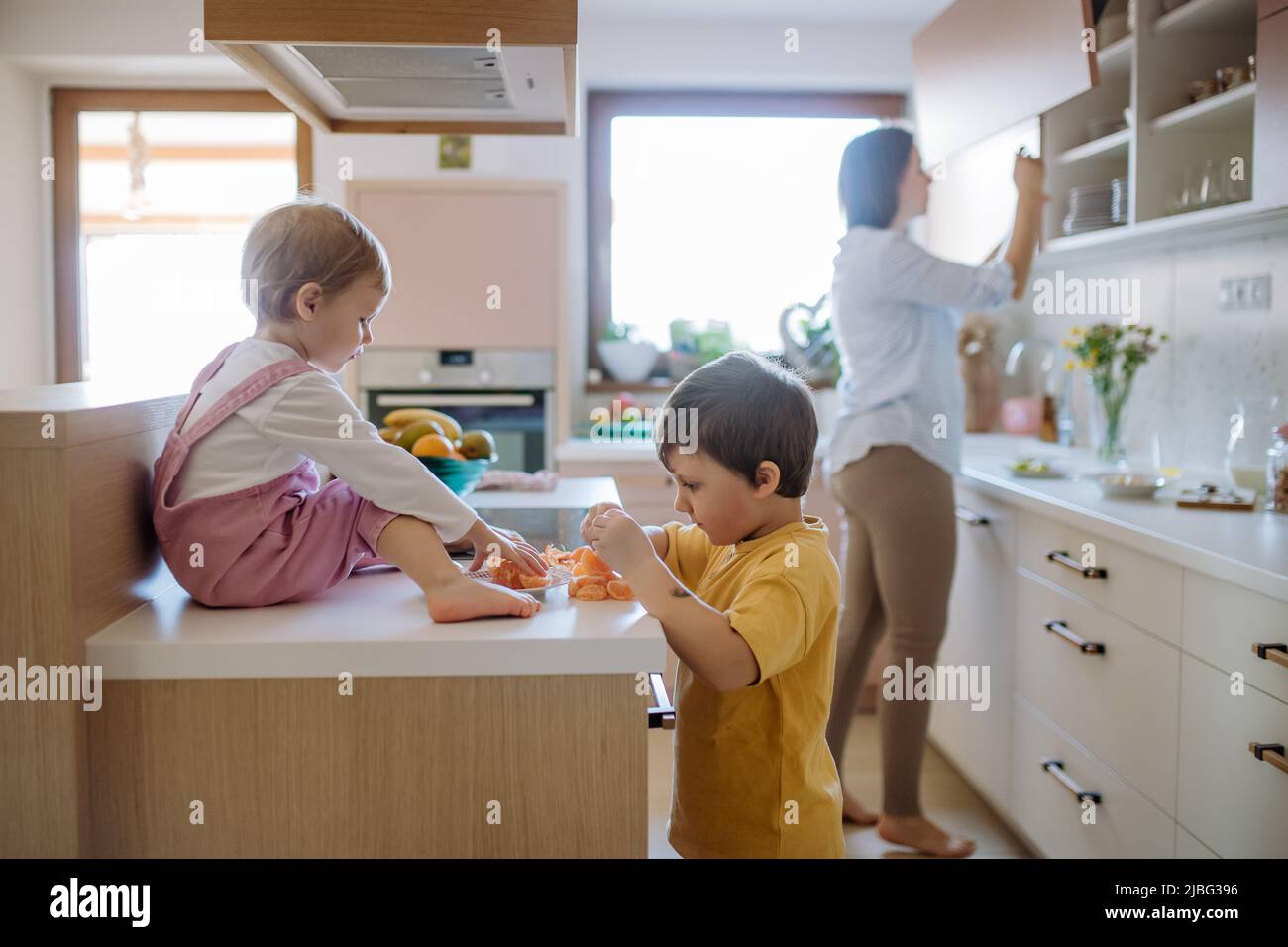 Mother of two little children preparing fruit snack in kitchen at home ...