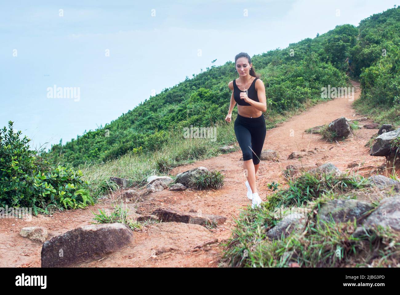 Sporty young woman in black sportswear trail running on mountain nature ...