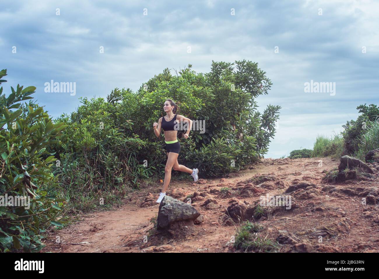 Young sportswoman cross country running on dirty rocky footpath in ...