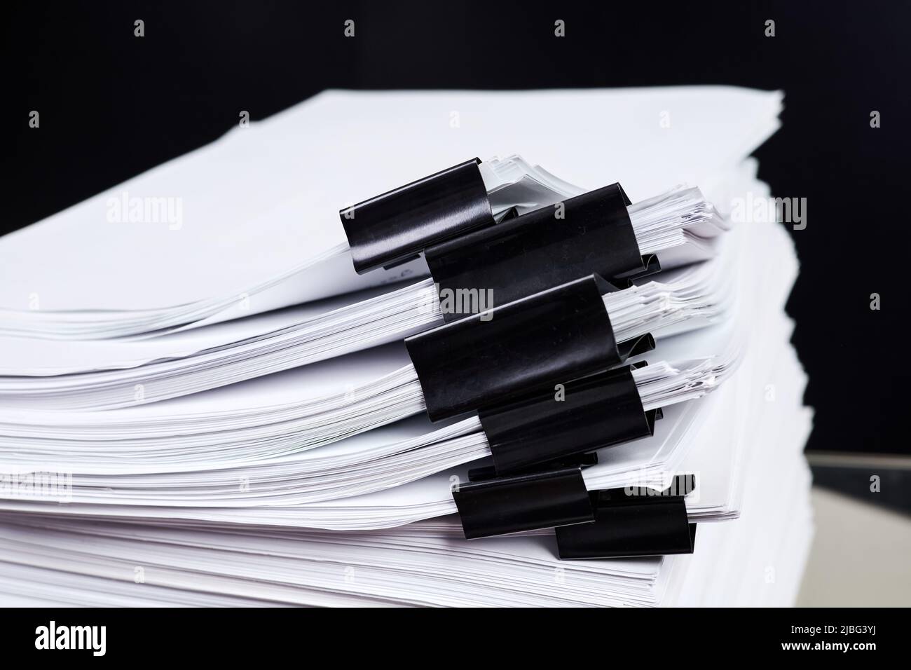 A stack of office papers, some of which are fastened with black binders ...