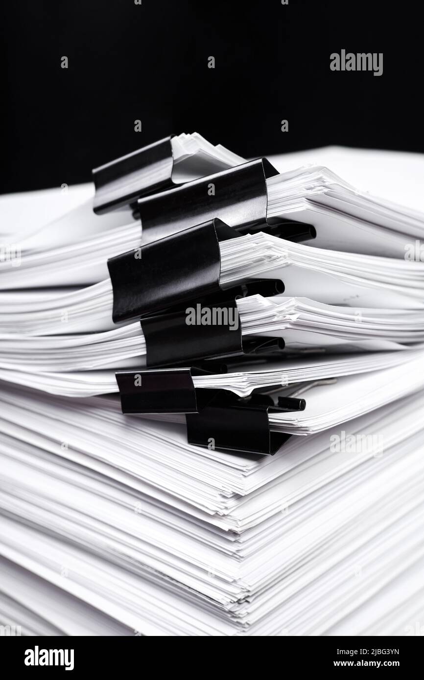 A stack of office papers, some of which are fastened with black binders ...