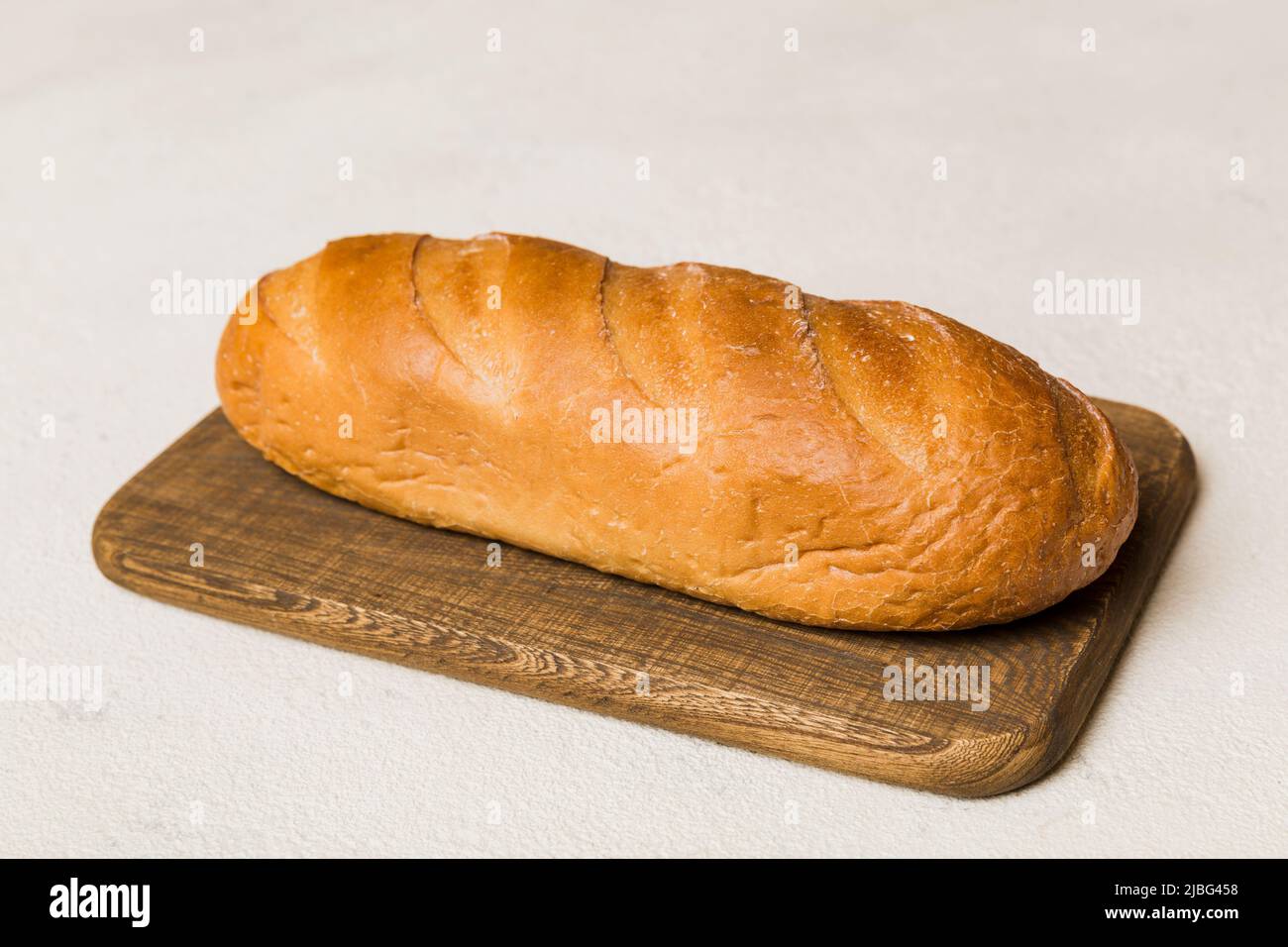 Freshly baked bread on cutting board against white wooden background ...
