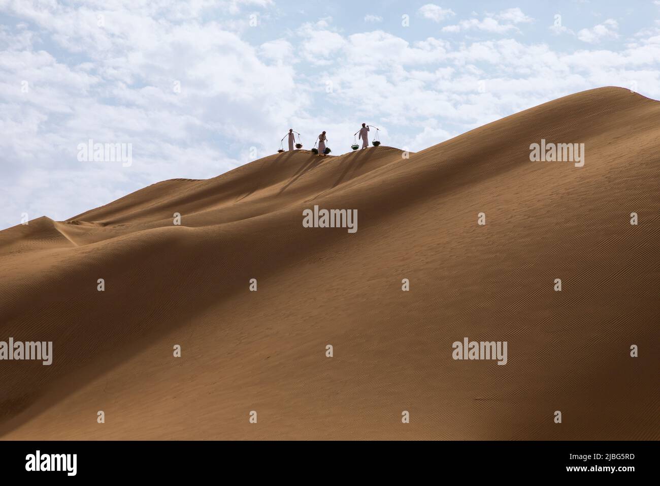 Omani men walking along the crest of a sand dune in the desert ...