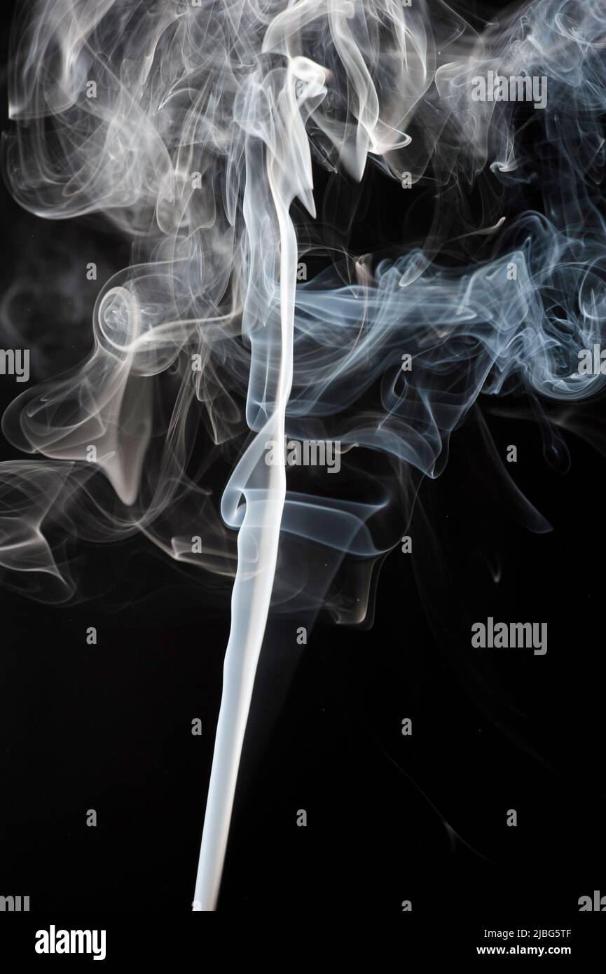 Puffs and curls of white smoke against a black background rising from a ...