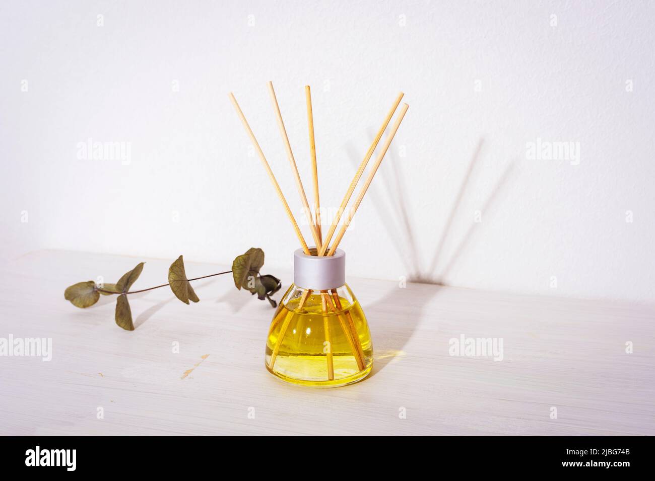 Glass bottle of aroma diffuser and eucalyptus branch on white wooden ...