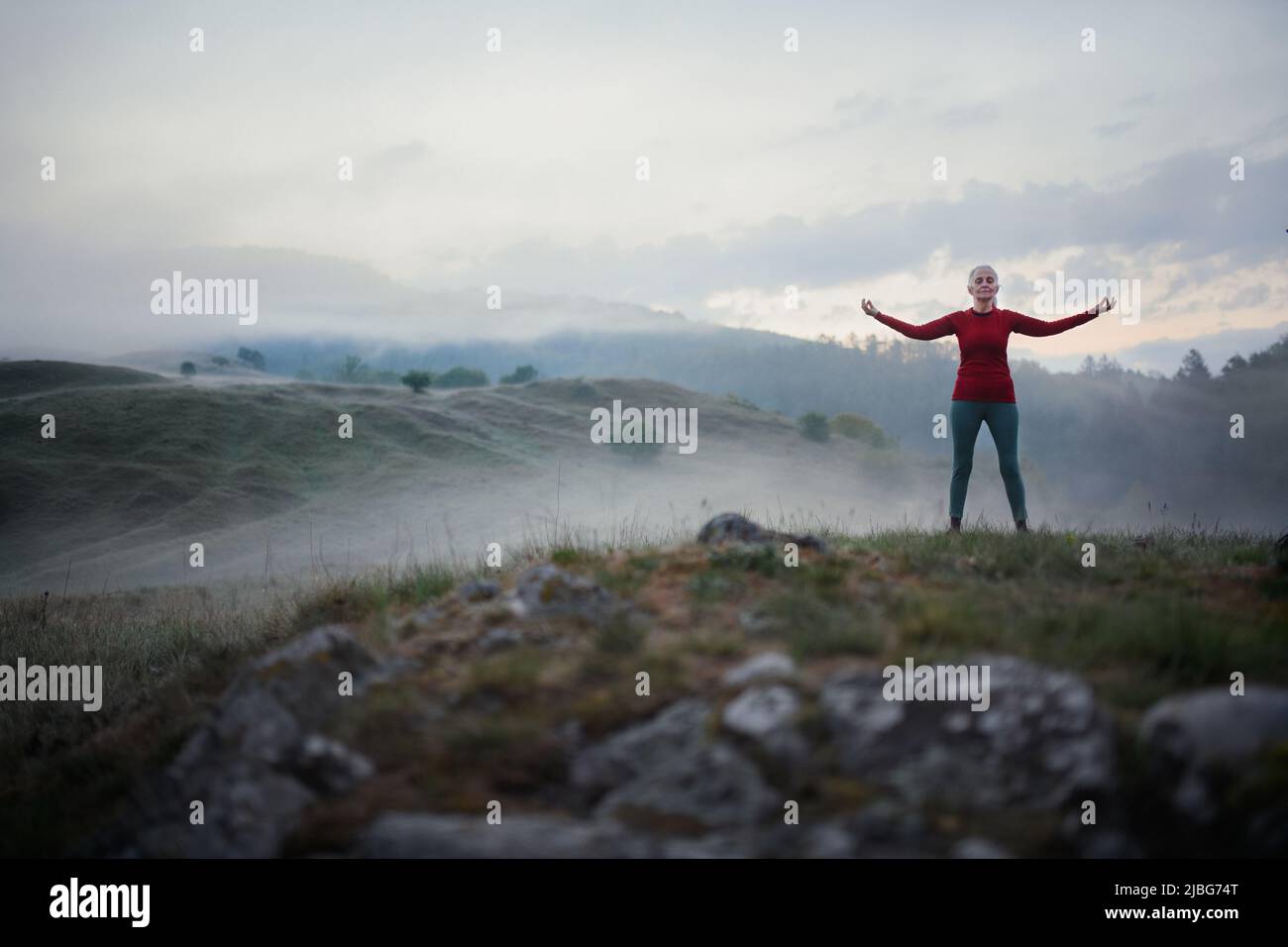 Senior woman doing breathing exercise in nature on early morning with ...