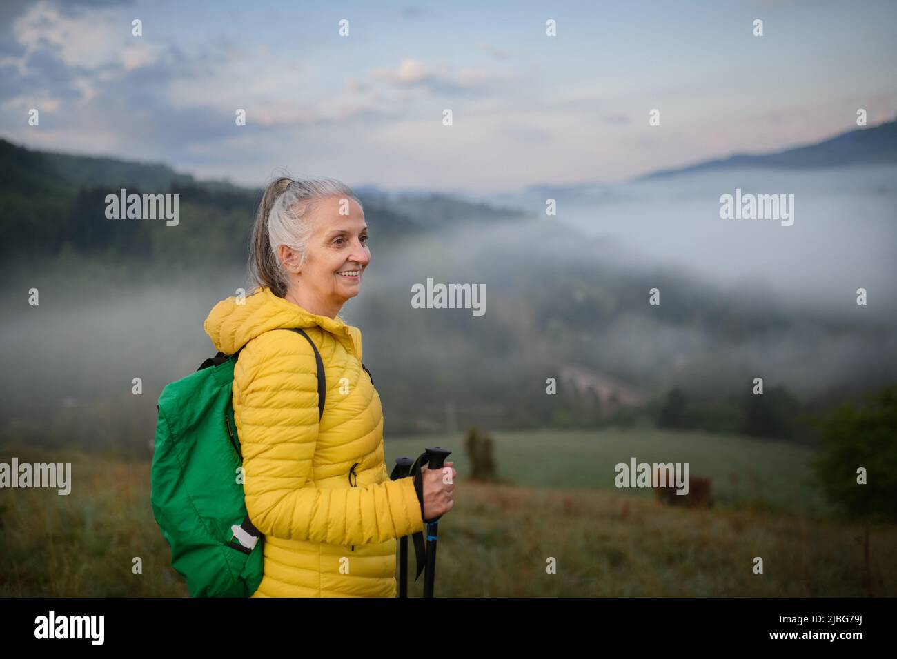 Senior woman hiking in nature on early morning with fog and mountains ...