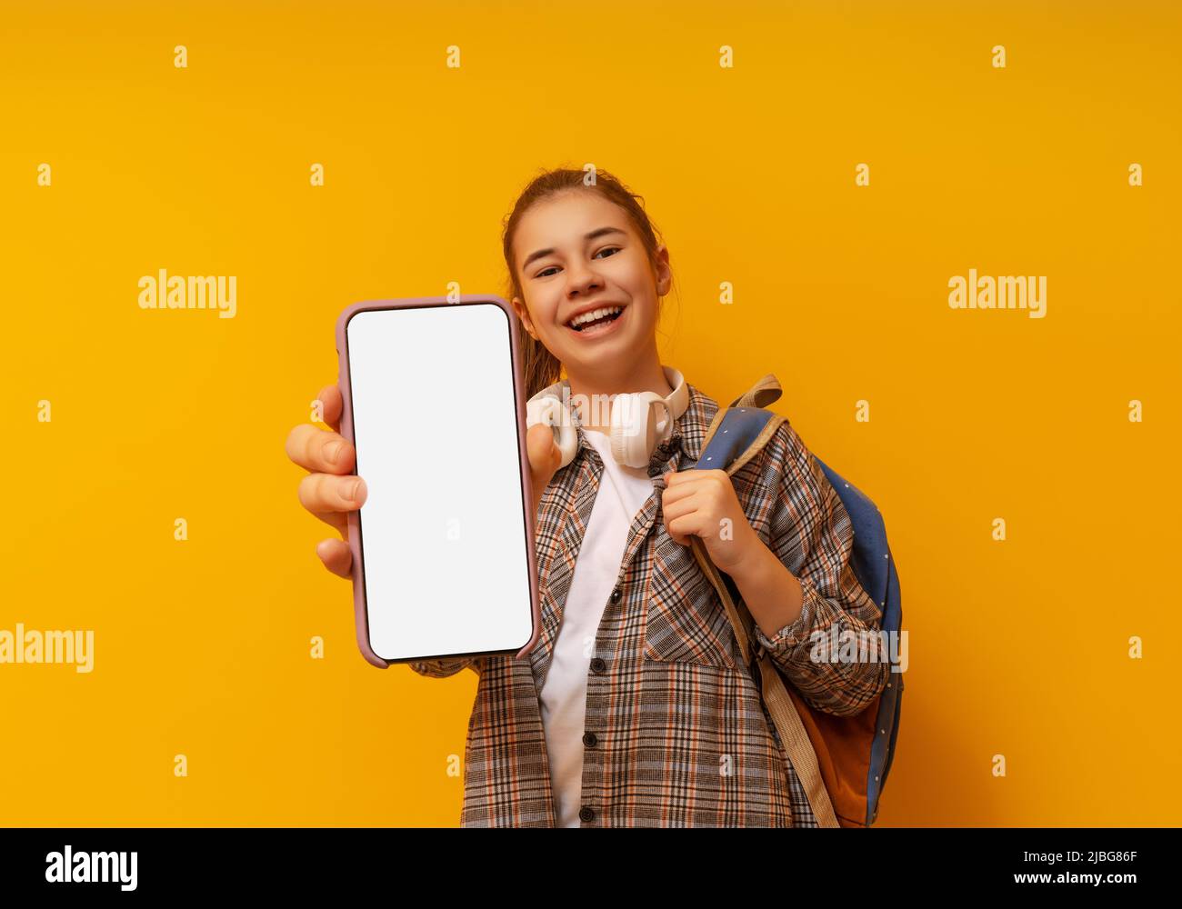 Happy school kid is showing smartphone on background of yellow wall ...