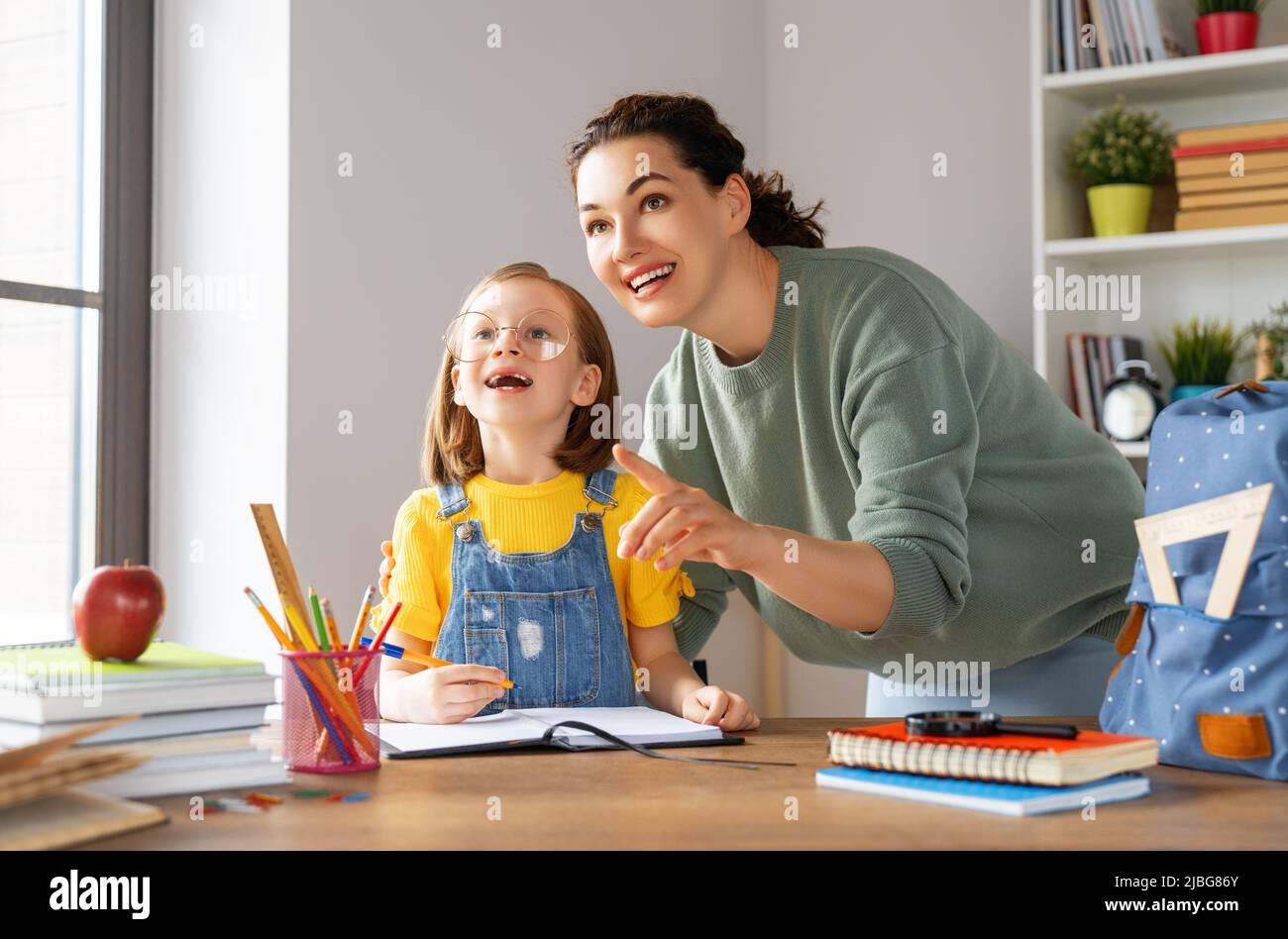 Happy child and adult are sitting at desk. Girl doing homework or ...