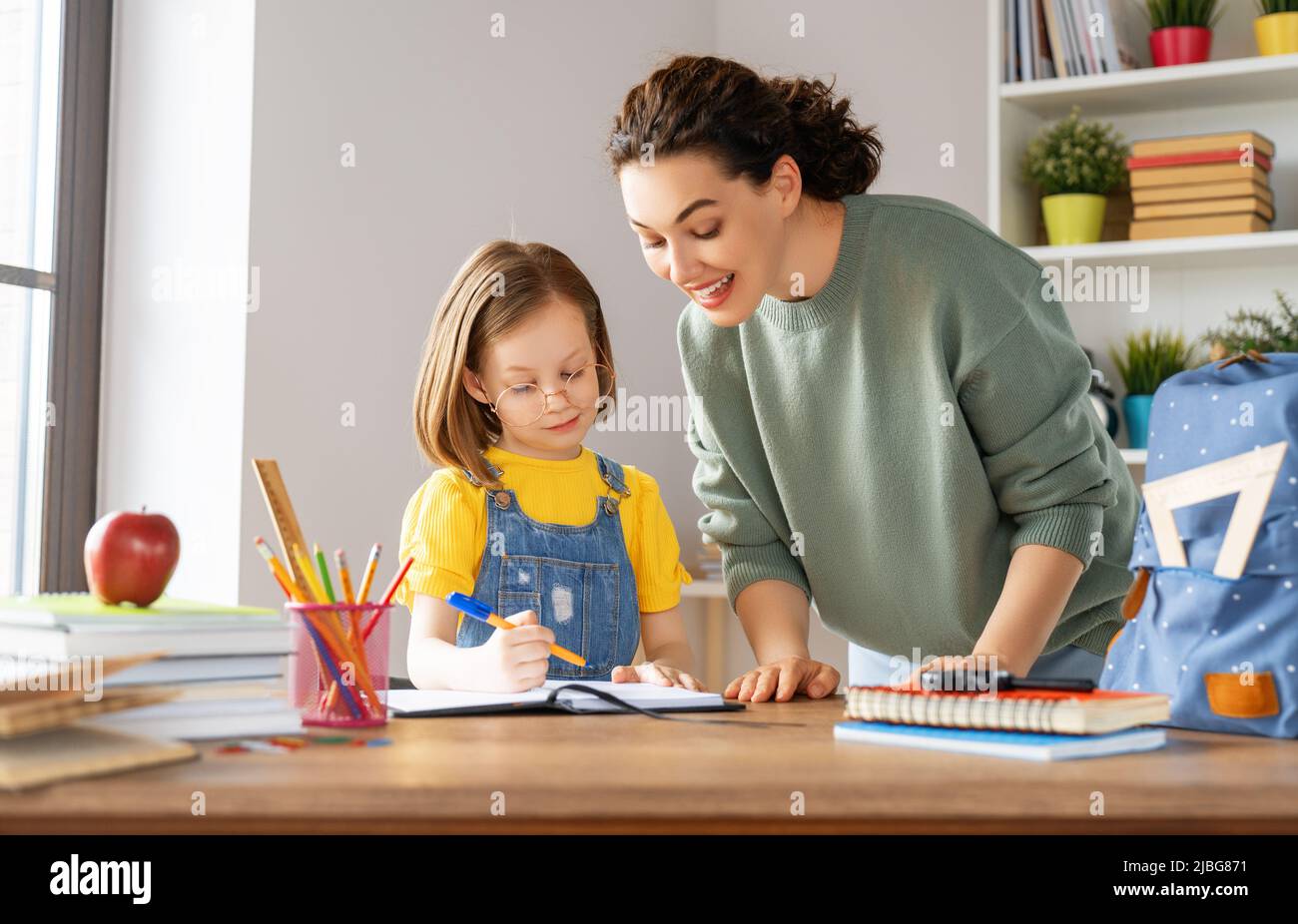 Happy child and adult are sitting at desk. Girl doing homework or ...