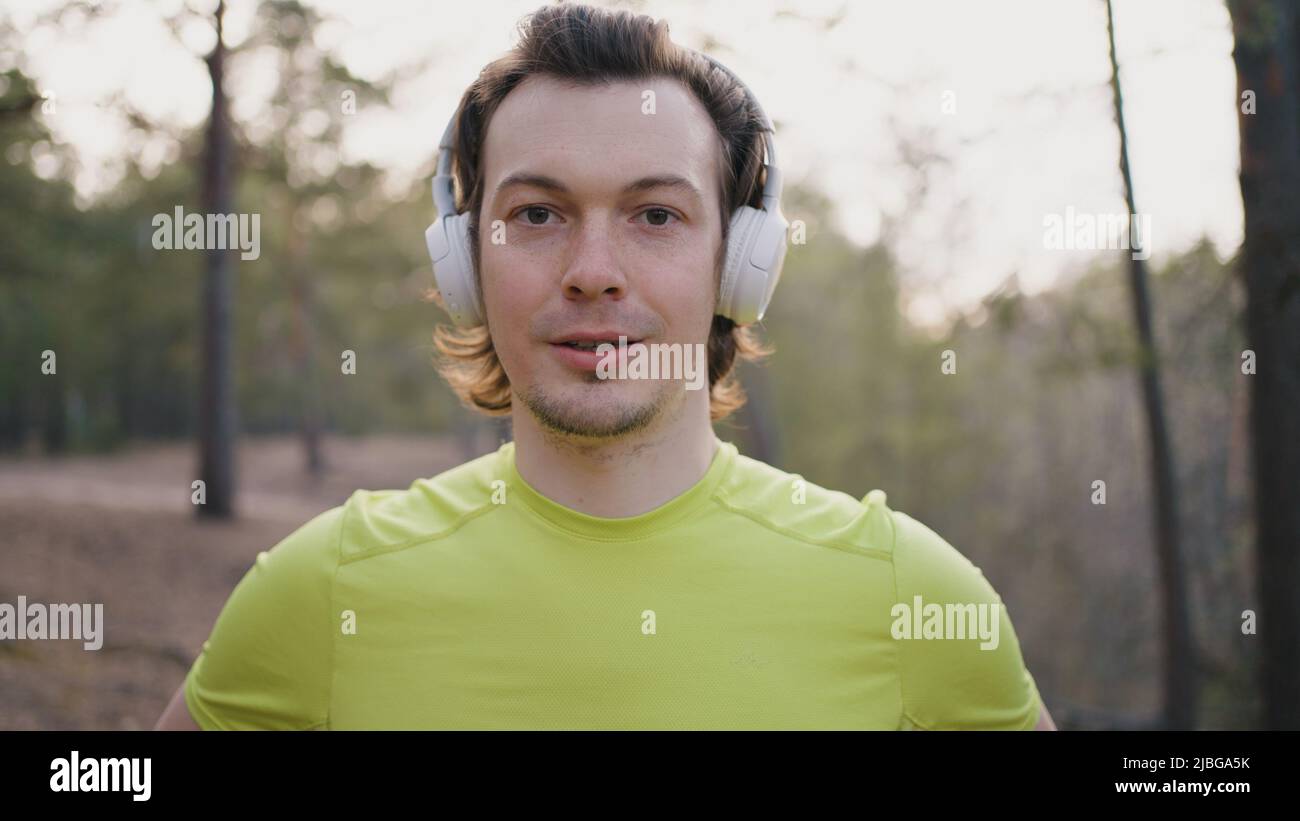 Young man at jogging takes break and looks at camera breathing deeply ...