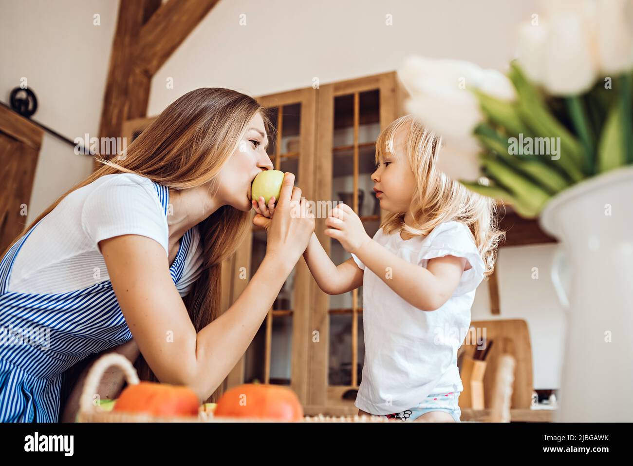 Little girl treats her mother to an apple at the kitchen Stock Photo ...