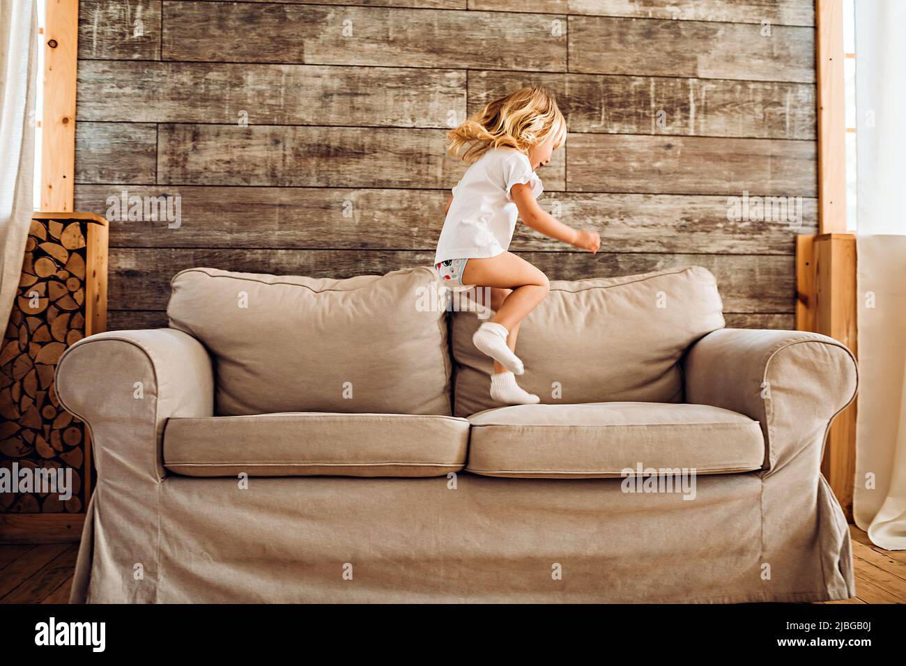 Lifestyle image of a little girl having fun and jumping on a sofa at ...