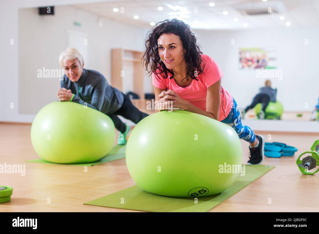 Two happy sportswomen exercising with a Swiss ball doing plank exercise ...