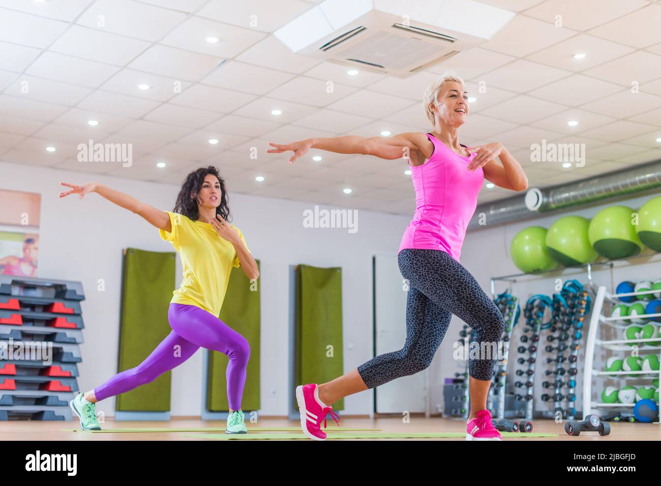 Two smiling female fitness models working out in gym or studio, doing cardio exercise, dancing ...