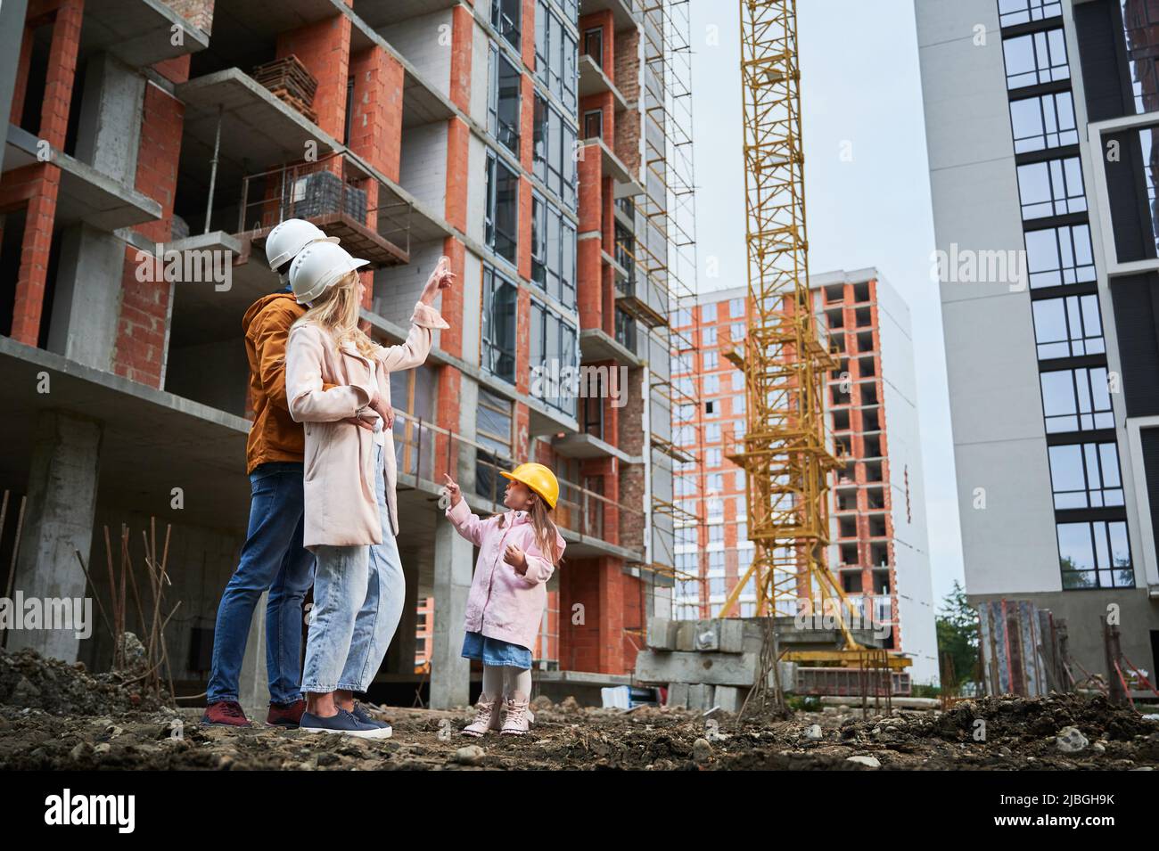 Man and woman in building helmets looking at tower crane while daughter ...