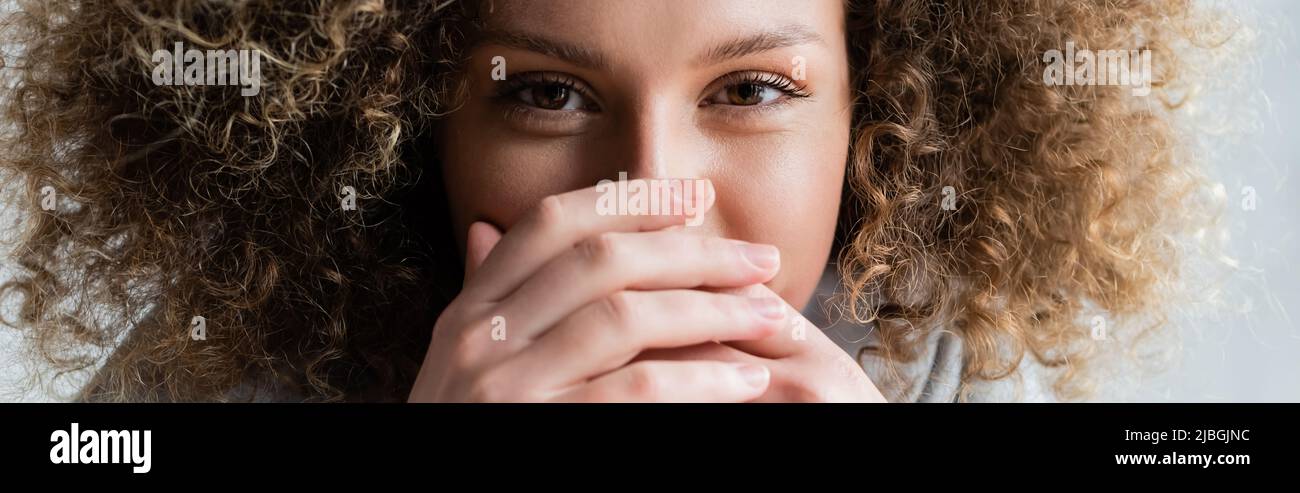 young curly woman with positive eye expression obscuring face with ...