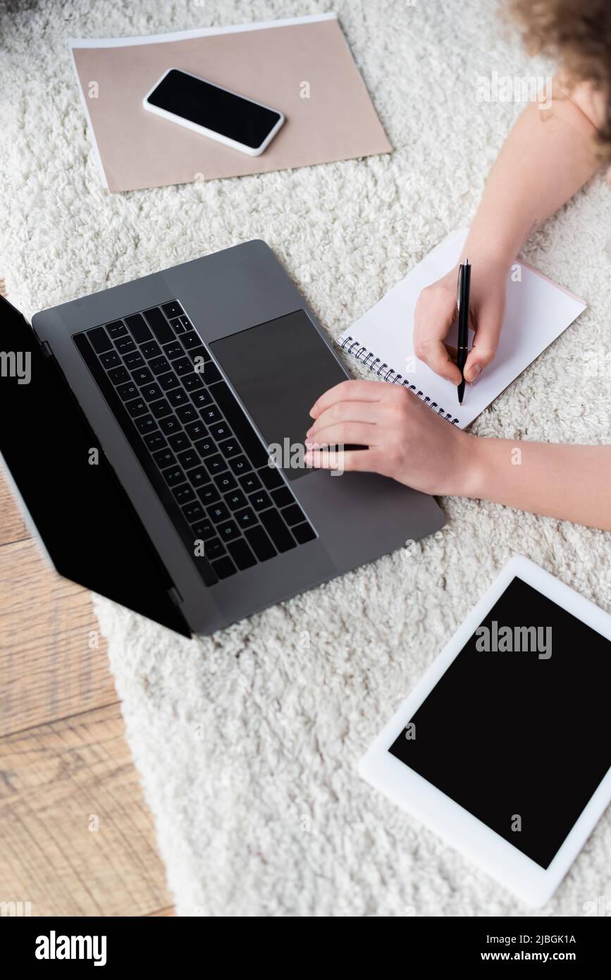 top view of cropped woman writing in notebook near devices with blank screen on floor Stock ...