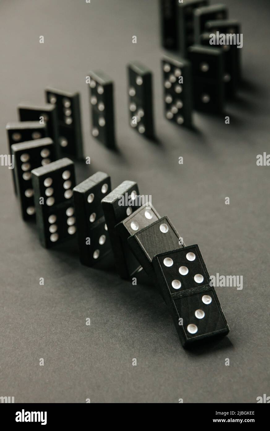 Black dominoes chain on a dark table background. Domino effect concept ...