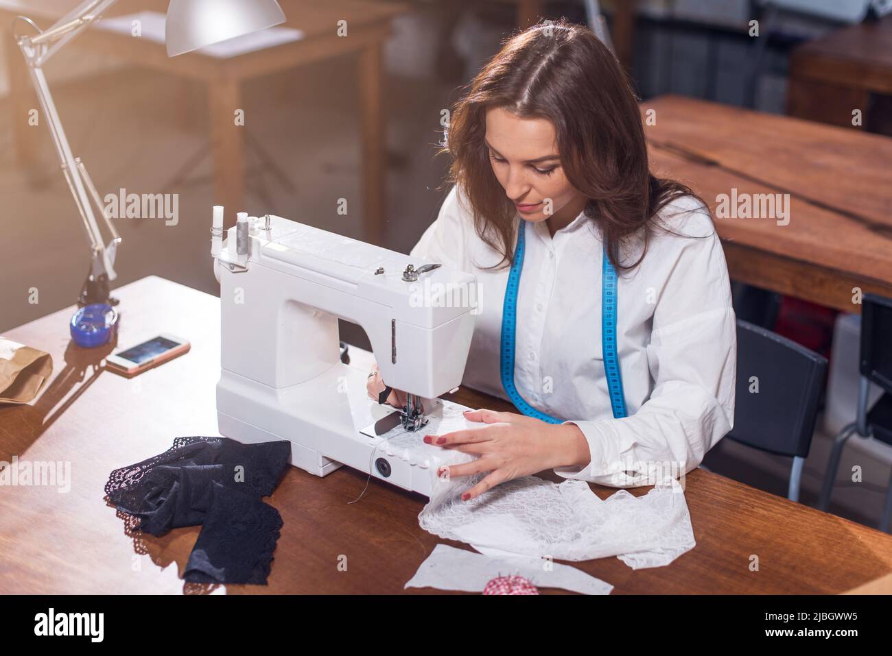 Female dressmaker working with sewing machine, stitching fabric sitting ...
