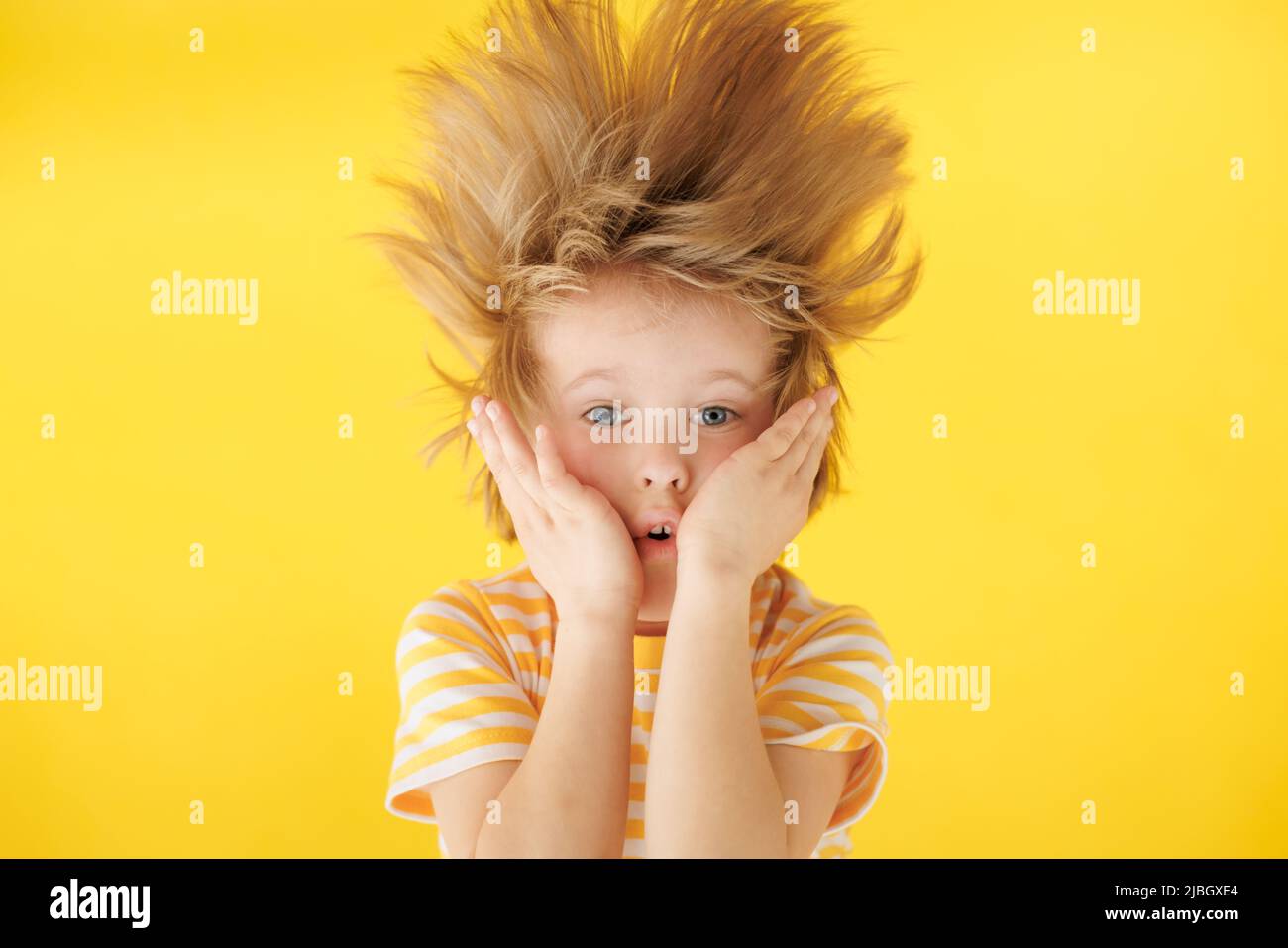 Surprised child holding face. Shocked kid against yellow background ...