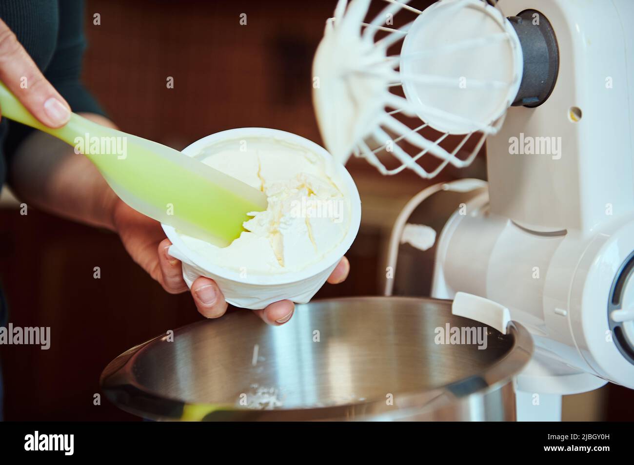 Close-up of a pastry chef's hands using a silicone spatula to put some ...