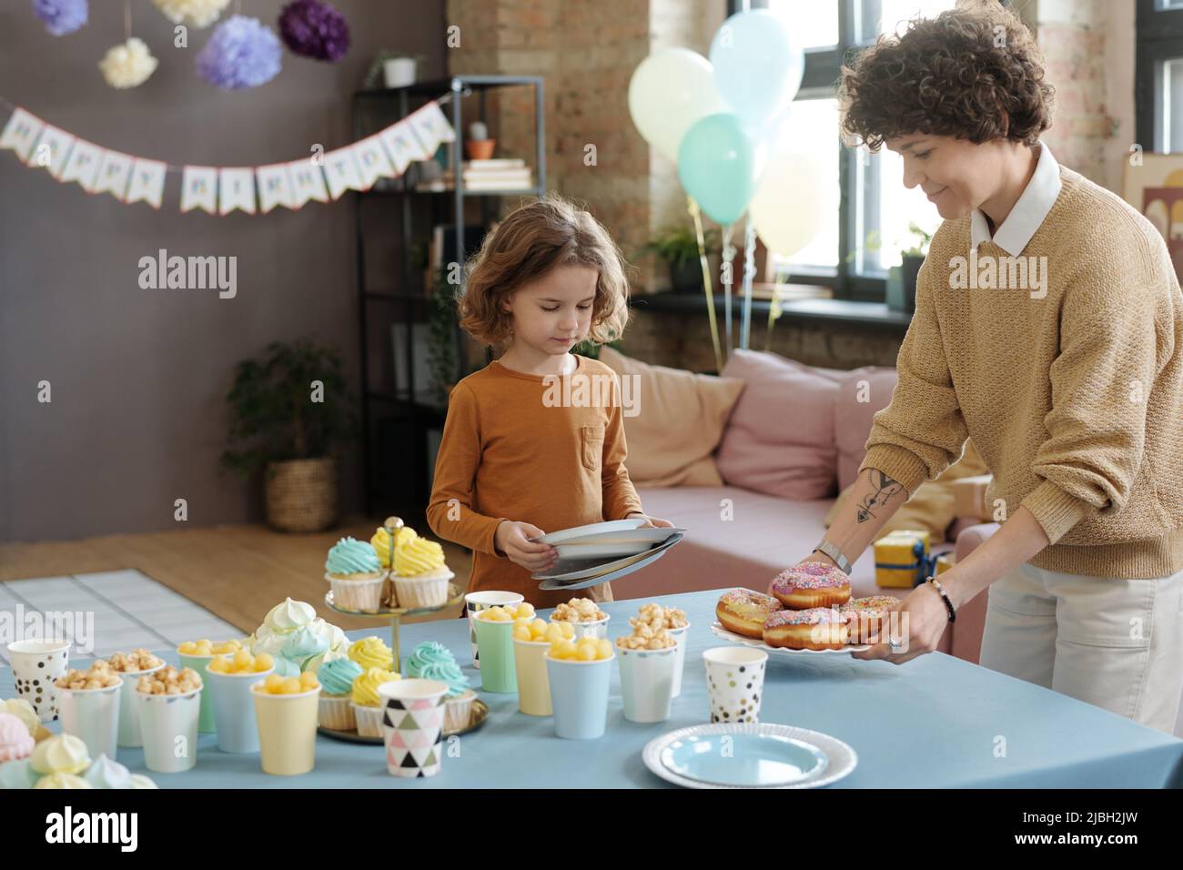 Little boy putting plates on table and helping his mother to set the ...