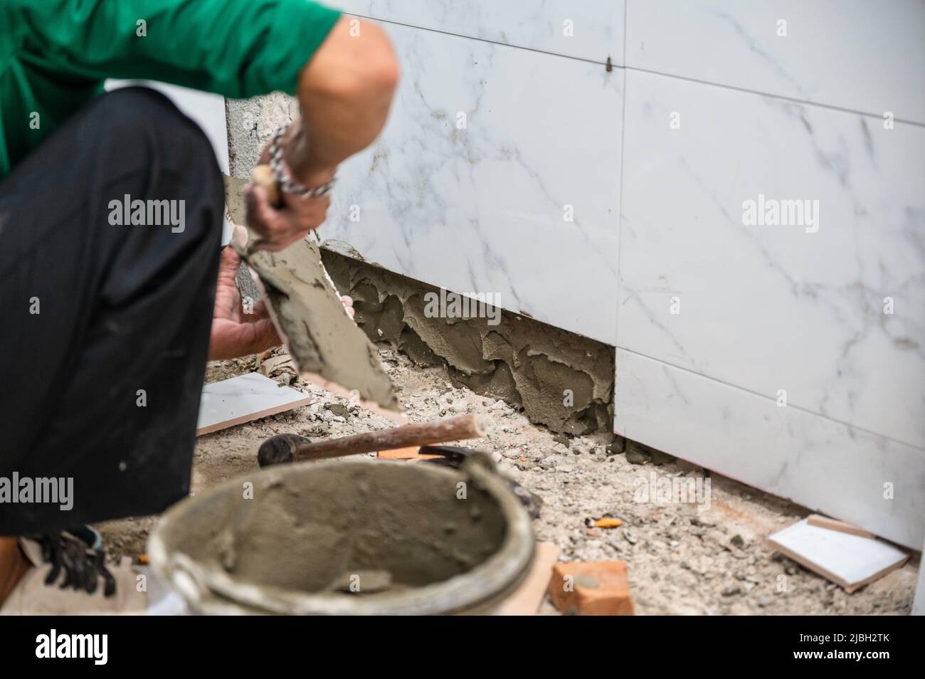 Male tiler using trowel laying marble tile with cement in bathroom ...