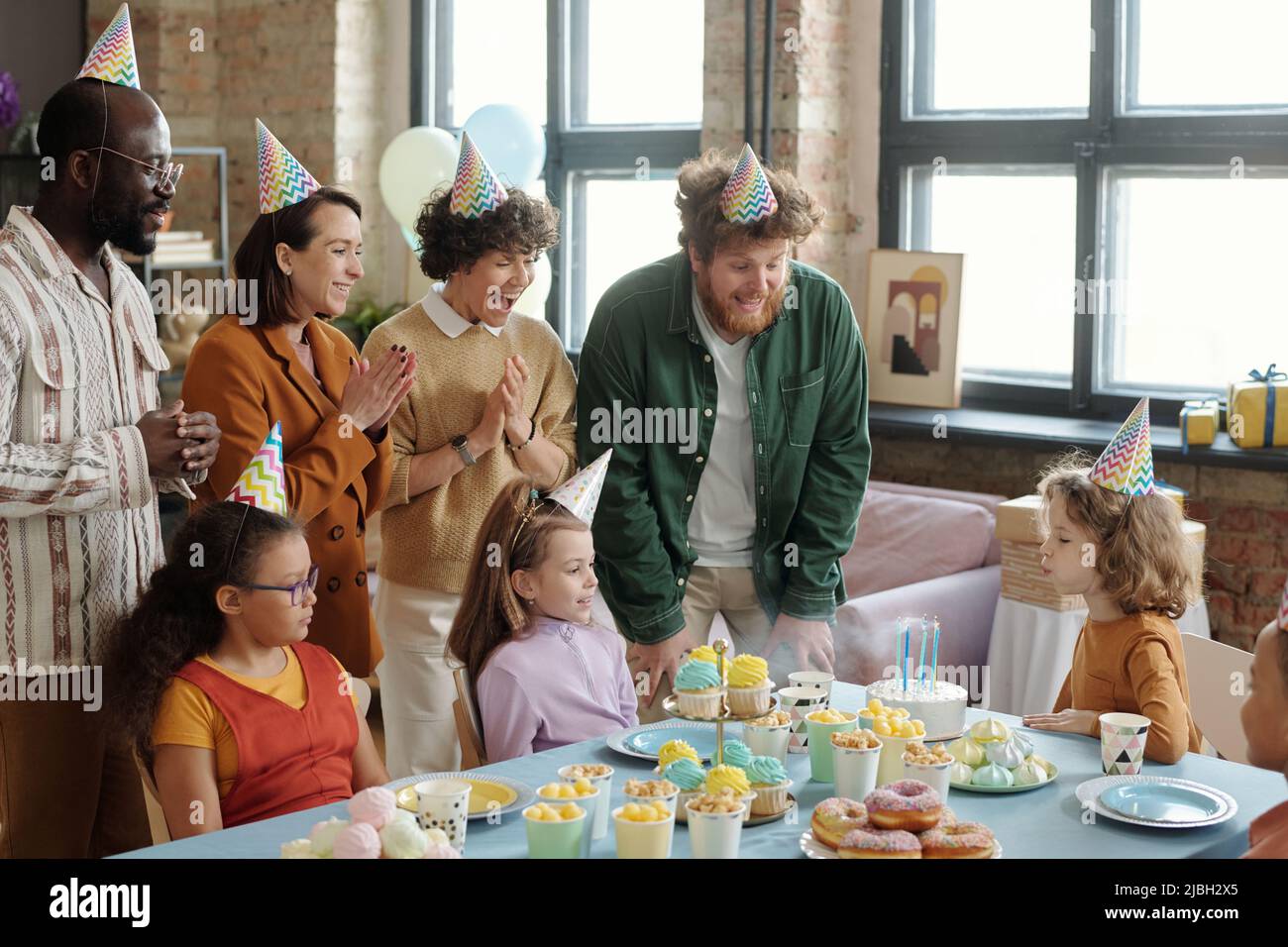 Group of children and adults in party hats clapping hands while little ...
