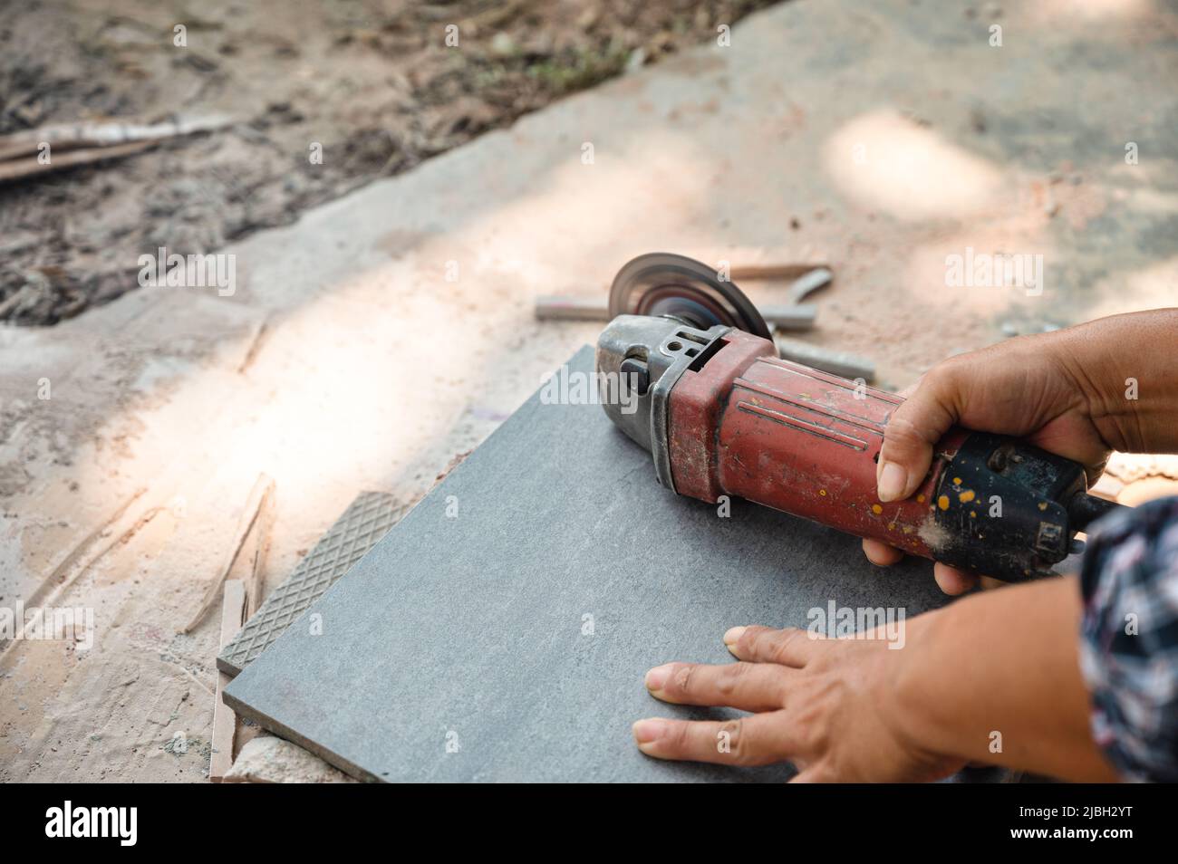 Worker using electric circular saw cutting granite tile in construction ...