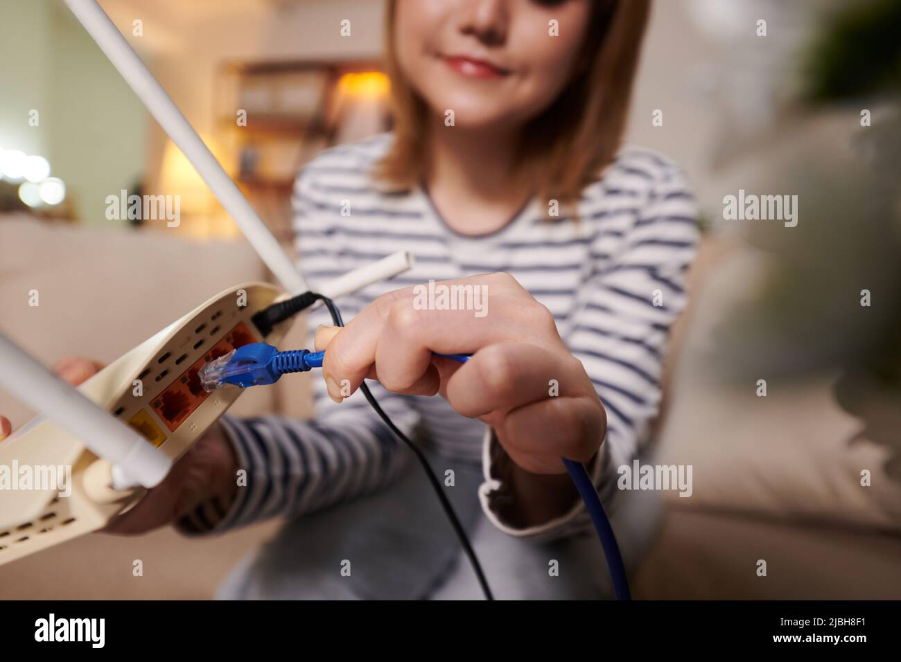 Closeup image of woman plugging Ethernet cord in back of modem to get ...
