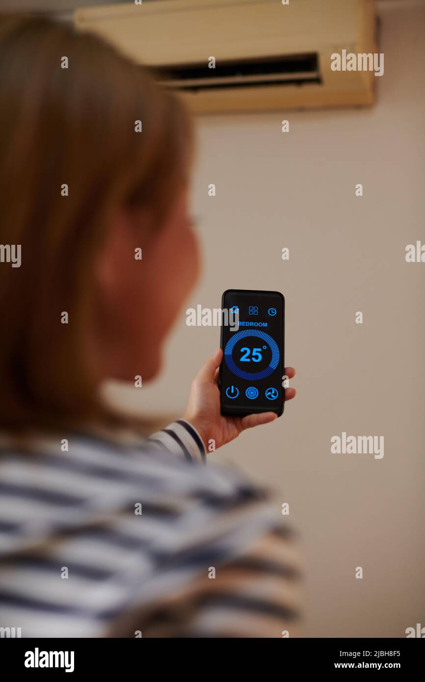 Young woman using application on smartphone to set temperature in ...